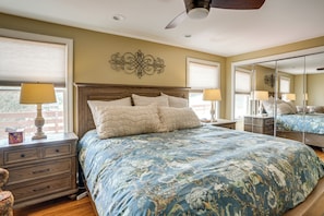 Quarto com uma cama grande, mesa de cabeceira, cômoda, espelho e ventilador de teto.
