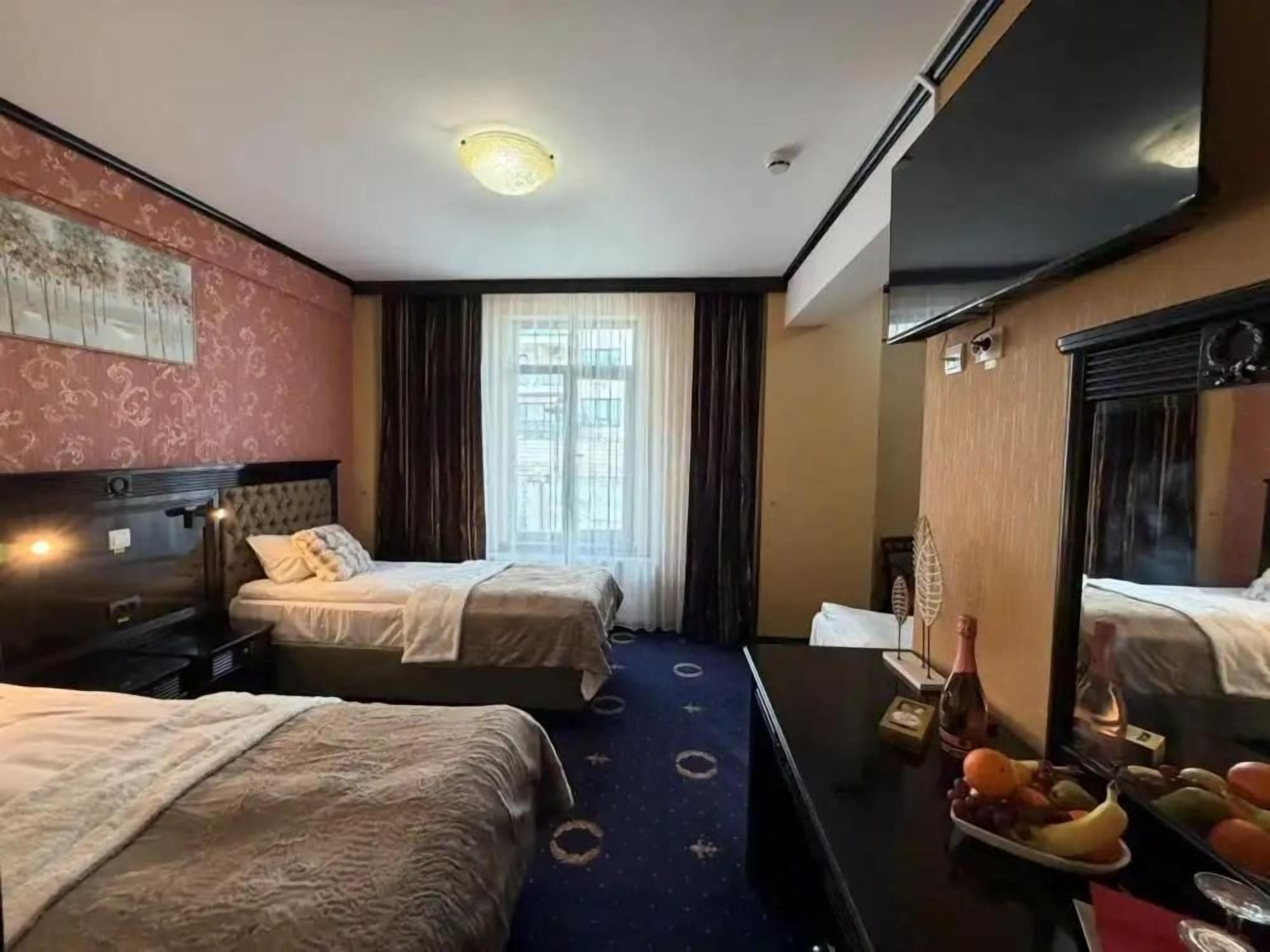 Quarto de hotel com duas camas, um espelho grande, uma mesa de jantar com frutas e vista para o exterior através de uma janela.