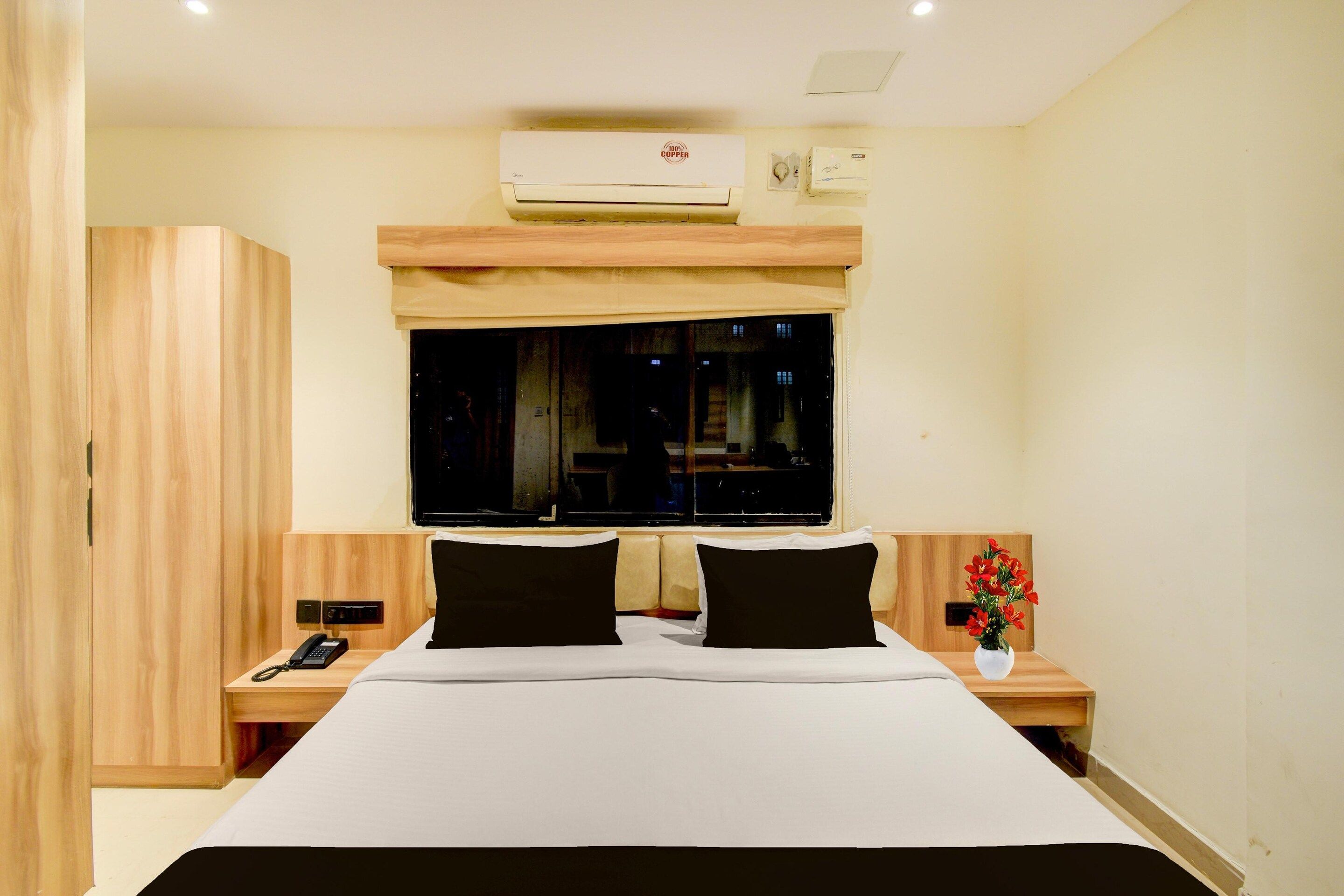 Quarto de hotel com uma cama grande, duas mesas de cabeceira, um guarda-roupa, uma janela com vista e um ar condicionado.