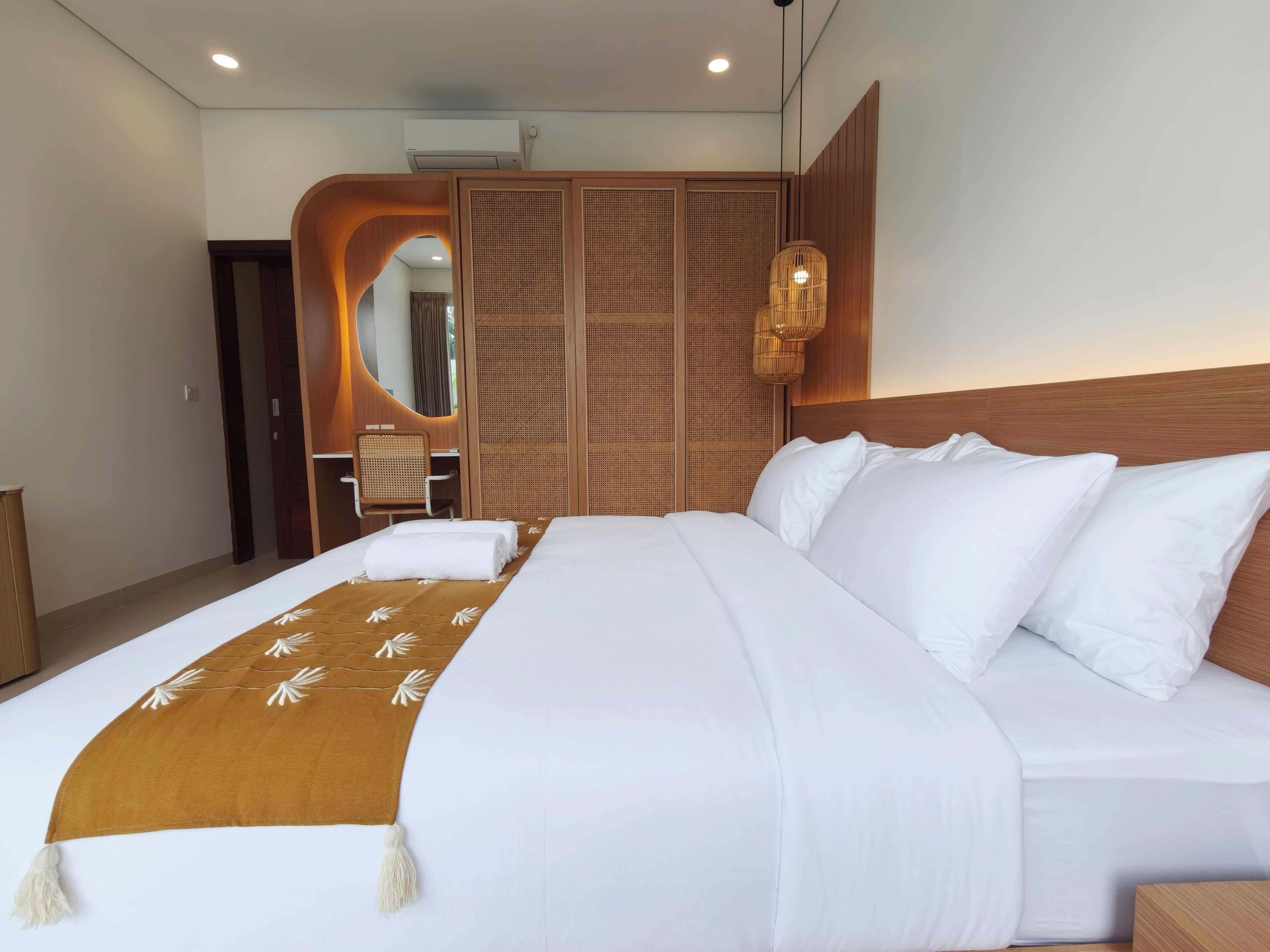 Quarto de hotel com uma cama grande, cabeceira de madeira, ar condicionado fixado na parede e divisória trançada.