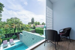 Uma varanda com piscina, duas cadeiras de vime e vista para o verde e edifícios.