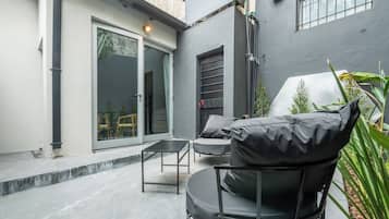 Uma área de estar moderna ao ar livre, com mesa, cadeiras, porta de correr de vidro e parede cinzenta.