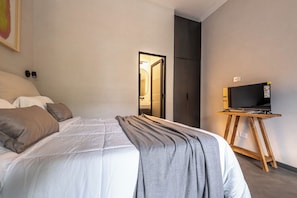 Quarto de hotel com uma cama, televisão sobre um suporte de madeira e um guarda-roupa.