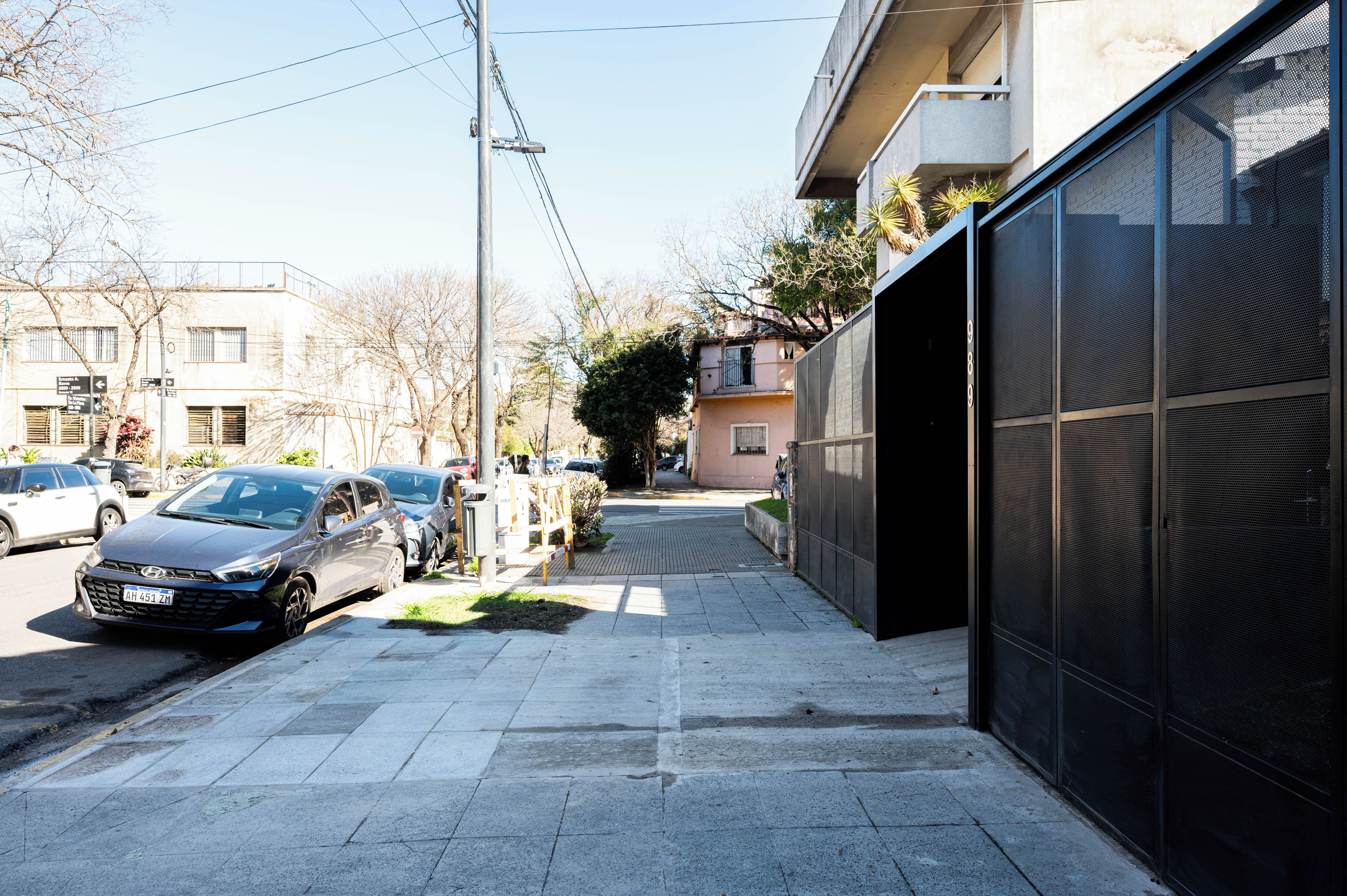 Rua residencial com carros estacionados, calçada e um edifício com cerca de metal.