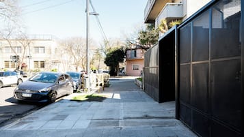 Rua residencial com carros estacionados, calçada e um edifício com cerca de metal.