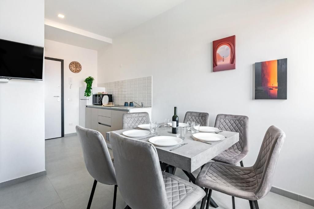 Uma sala de jantar moderna com uma mesa retangular posta para seis pessoas, cadeiras cinzas estofadas, uma TV de tela plana na parede e obras de arte nas paredes.