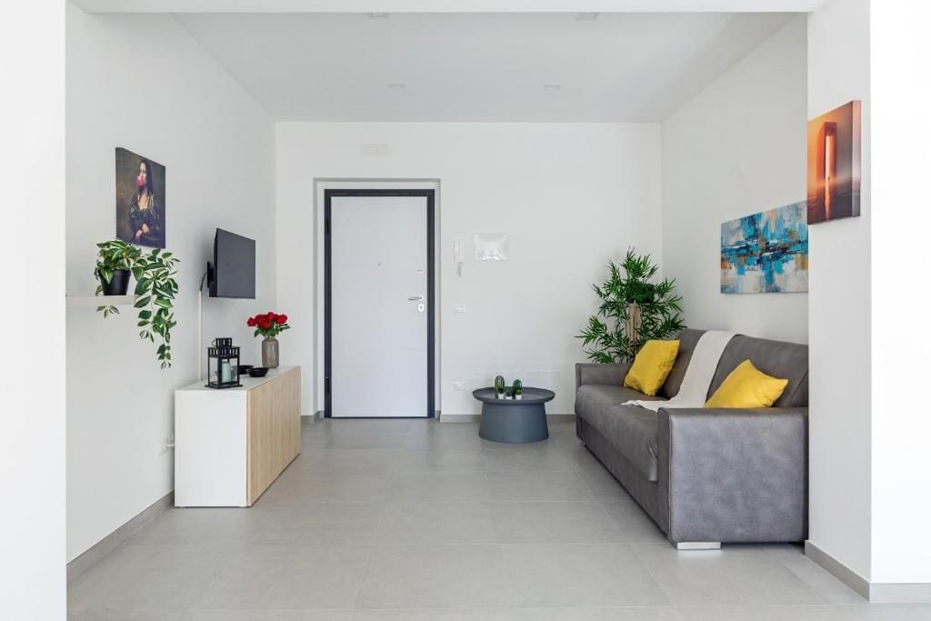 Uma sala de estar moderna com um sofá cinzento, uma pequena mesa de centro redonda e um armário branco com plantas.