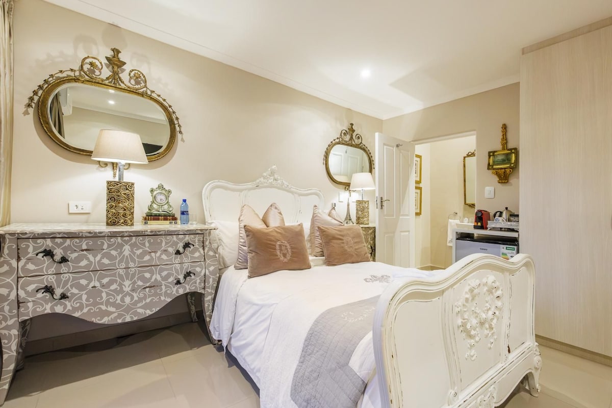 Quarto com uma cama grande, duas mesas de cabeceira com luminárias, um espelho e um guarda-roupa.