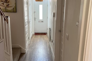 Corredor com piso de madeira, portas brancas e uma porta no final que dá para um quarto.