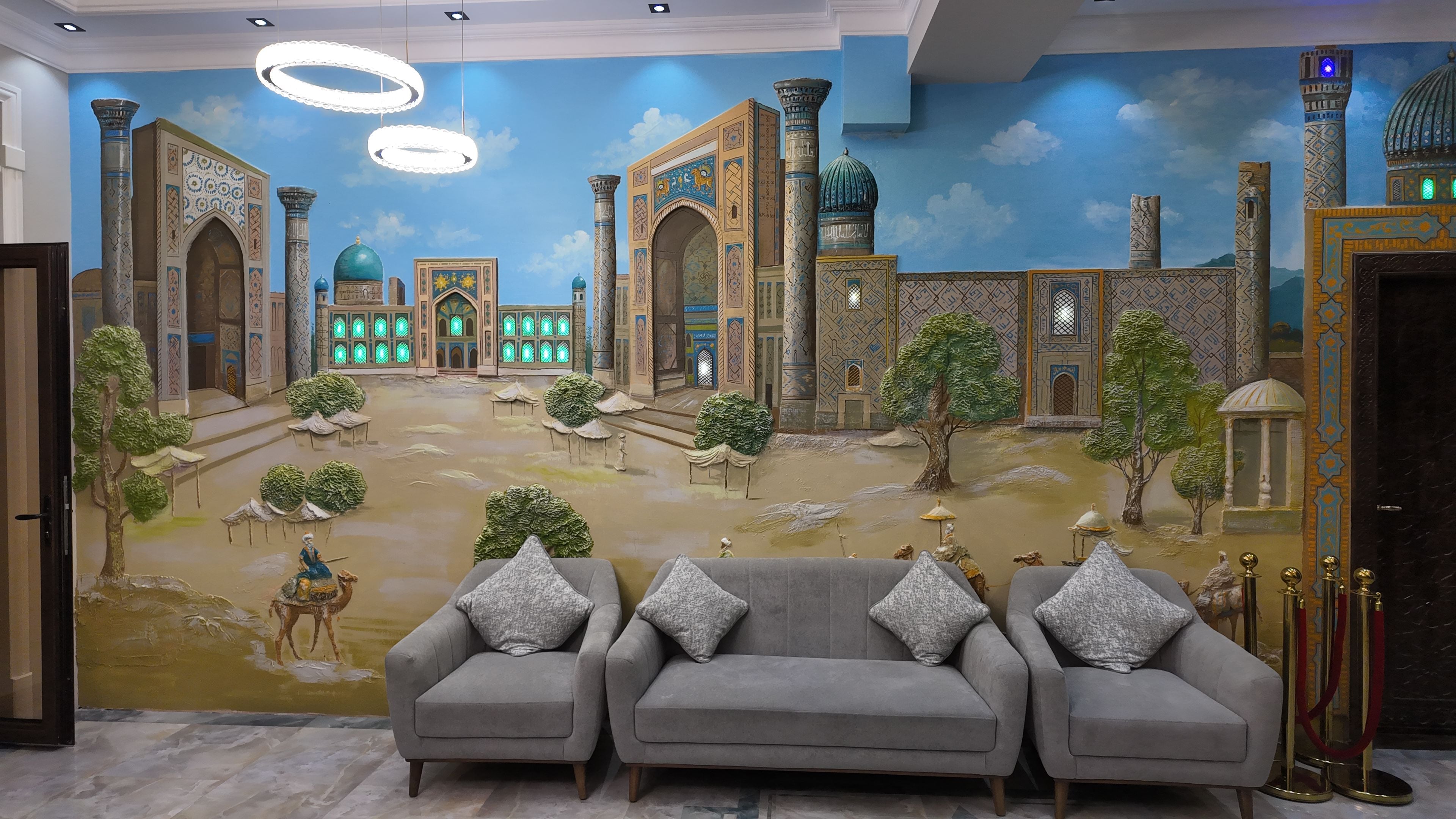 Quarto com um mural de um edifício histórico, um sofá cinzento e um candelabro.