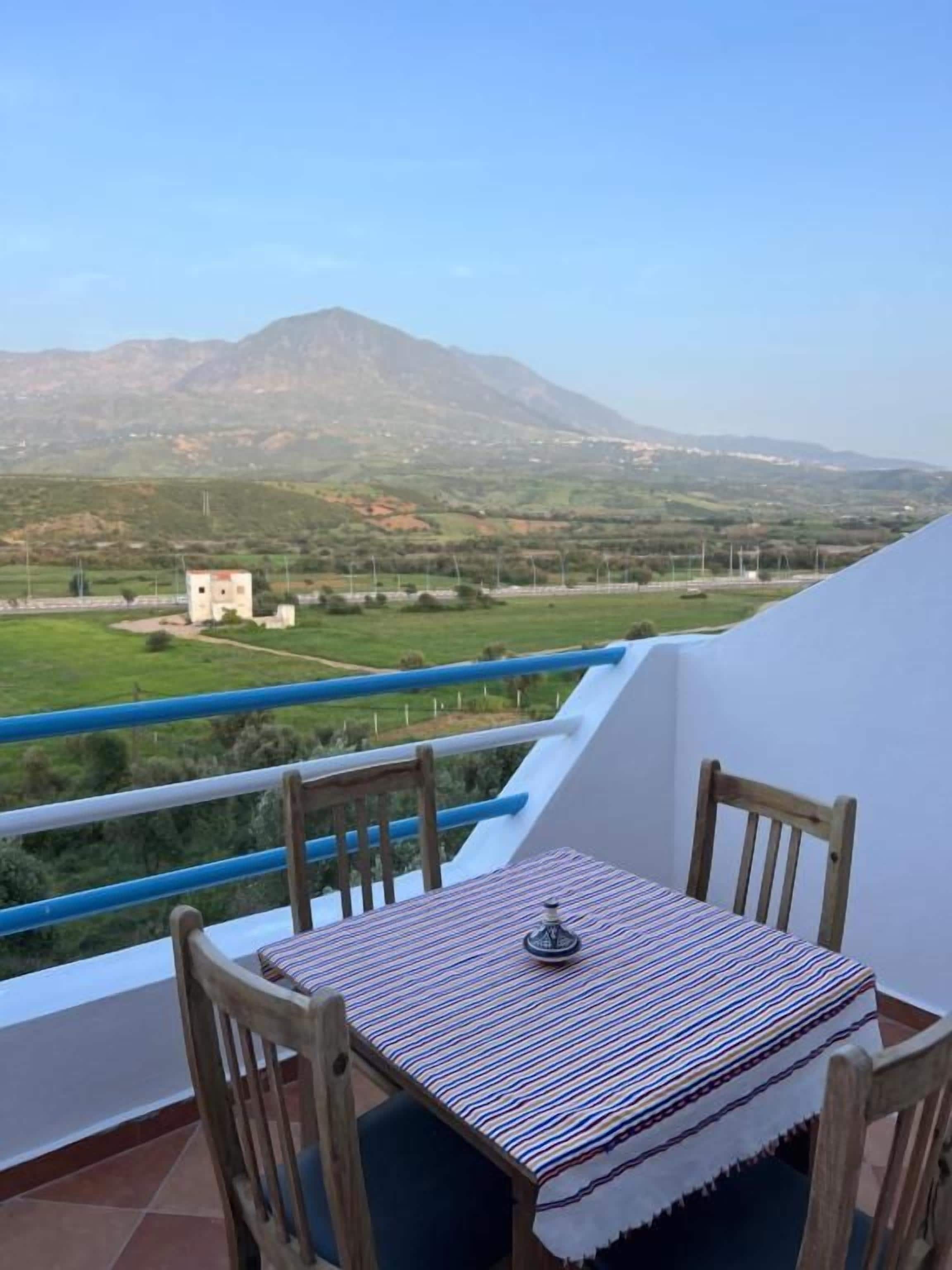 Varanda com mesa e cadeiras, com vista para uma paisagem montanhosa.