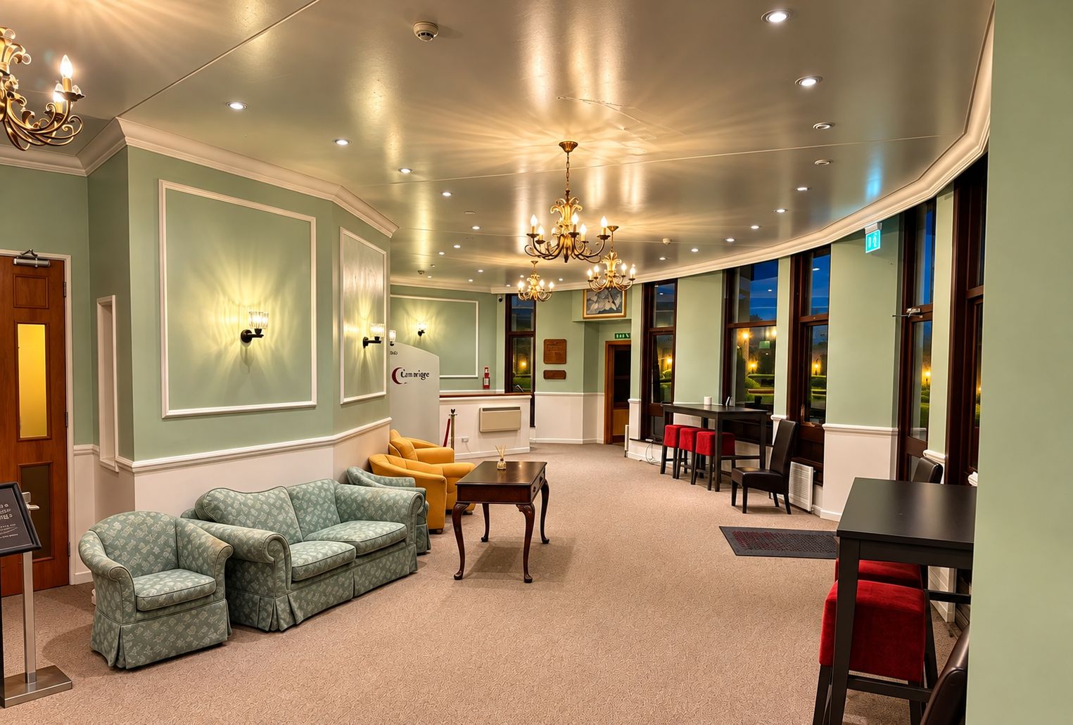 Um saguão de hotel com teto curvo, área de estar com sofás e poltronas, balcão de recepção e grandes janelas.