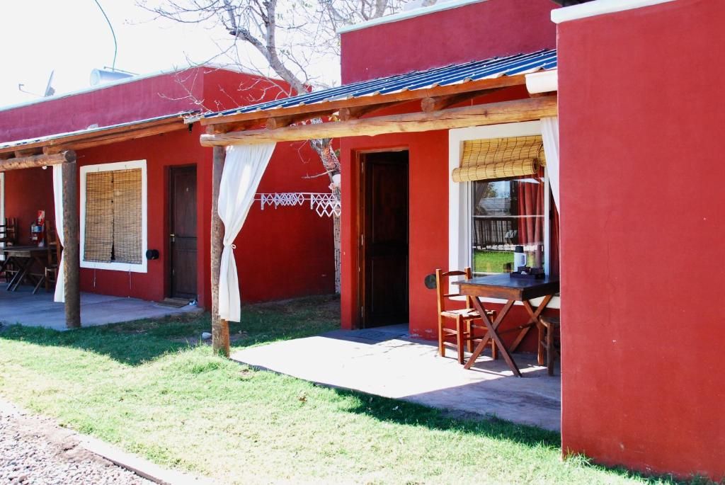 Um edifício vermelho com um alpendre coberto, uma mesa com cadeiras e uma janela com cortina.