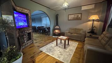 Uma sala de estar acolhedora com lareira, piso de madeira, um sofá, uma mesa de centro e uma televisão.