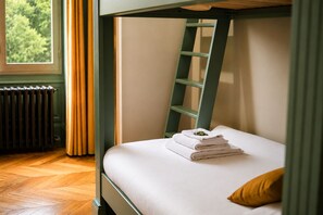Uma cama box com escada, um radiador e uma janela com cortinas.