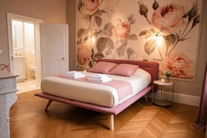 Quarto com cama, mesa de cabeceira e parede decorada com papel de parede floral.