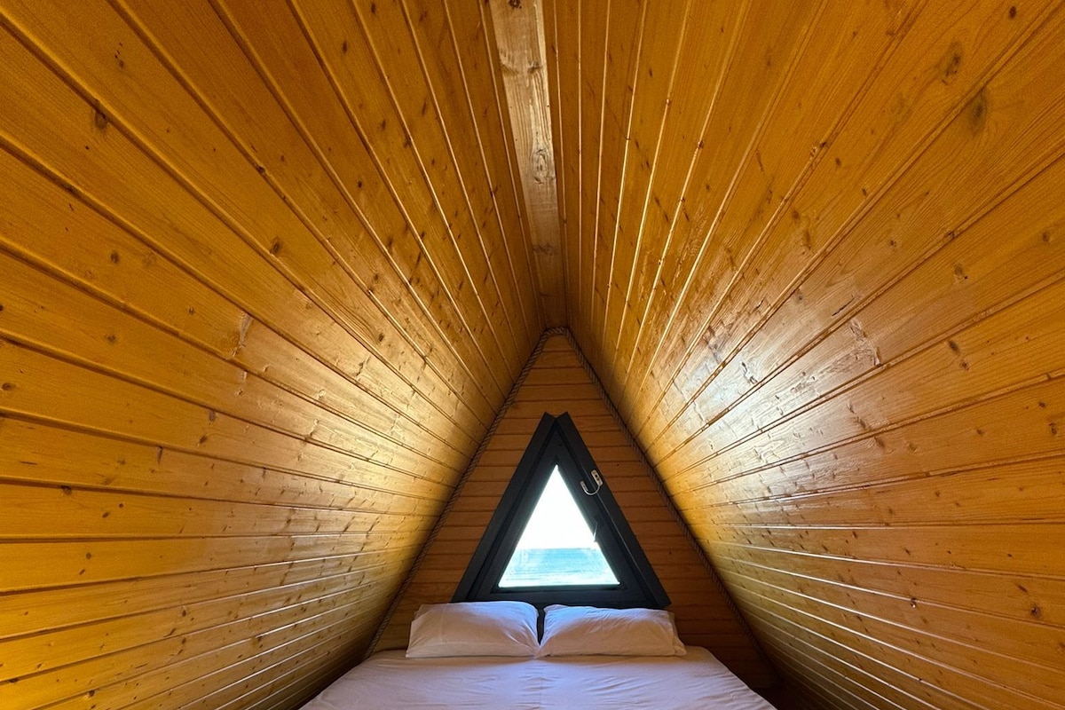Quarto triangular com uma cama centralizada sob um claraboia.