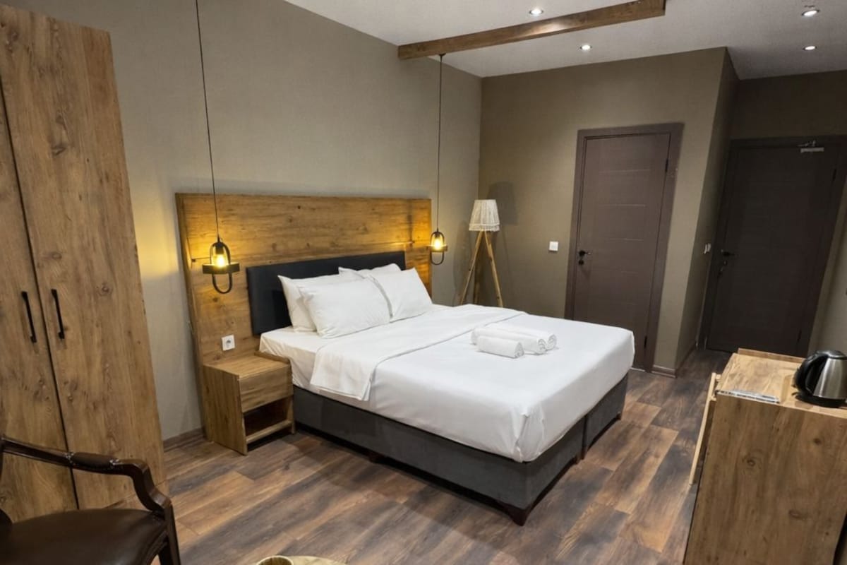 Quarto moderno com uma cama grande, cabeceira de madeira, mesas de cabeceira, uma mesa de centro redonda e um guarda-roupa.