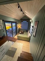 Um interior aconchegante com um sofá verde, piso de madeira e vista pela janela com persianas.