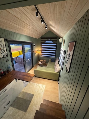 Um interior aconchegante com um sofá verde, piso de madeira e vista pela janela com persianas.