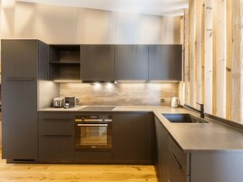 Uma cozinha moderna com armários escuros, forno embutido e pia de aço inoxidável.