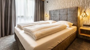 Quarto de hotel com uma cama grande, cortinas, cabeceira e iluminação fixada na parede.