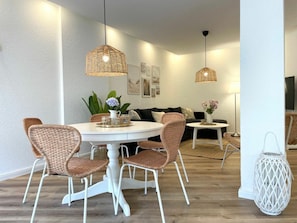 Uma área de refeições com mesa redonda, cadeiras brancas e luminárias pendentes de vime.