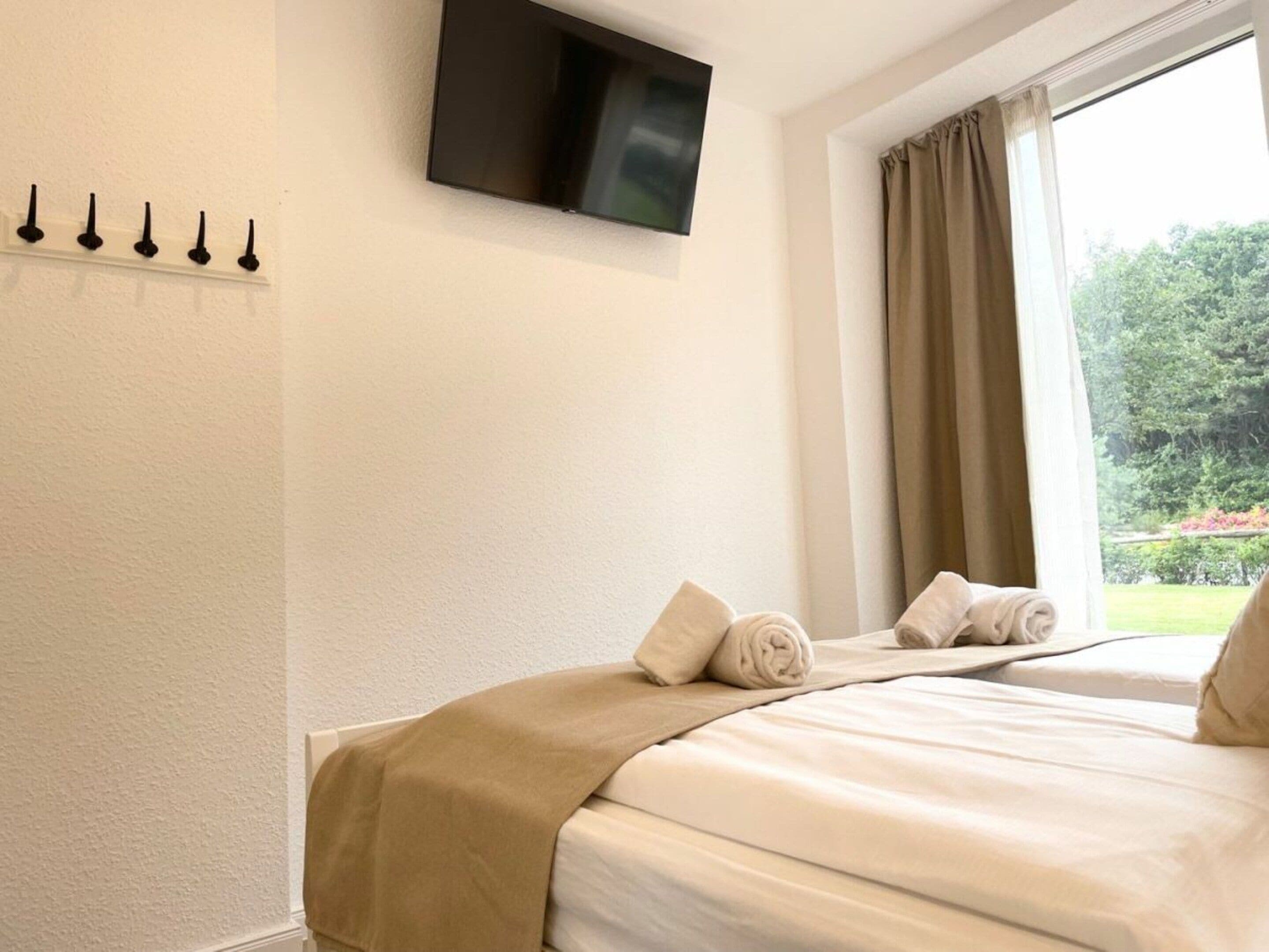 Quarto de hotel com cama, TV de tela plana na parede e janela com cortinas.