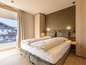 Quarto moderno com cama grande, cabeceira de madeira e vista para um estacionamento.