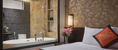 Quarto de hotel com uma cama grande, banheiro com banheira e espelho.