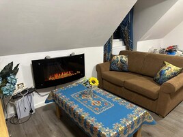 Uma sala de estar com sofá, mesa de centro, televisão de tela plana e lareira.