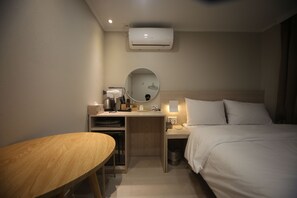 Quarto de hotel com cama, escrivaninha com espelho, espelho redondo, mesa e ar condicionado.
