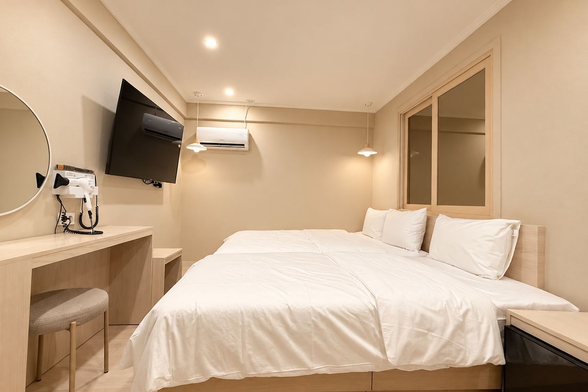 Quarto de hotel com cama, escrivaninha com secador de cabelo, televisão de tela plana e espelho grande.