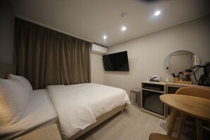 Quarto de hotel com cama, escrivaninha, cadeira, televisão e espelho.