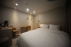 Quarto de hotel com cama, escrivaninha, cadeira, mesa e um cabideiro.