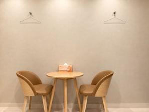 Quarto com duas cadeiras e uma pequena mesa redonda, com dois cabides fixados na parede.