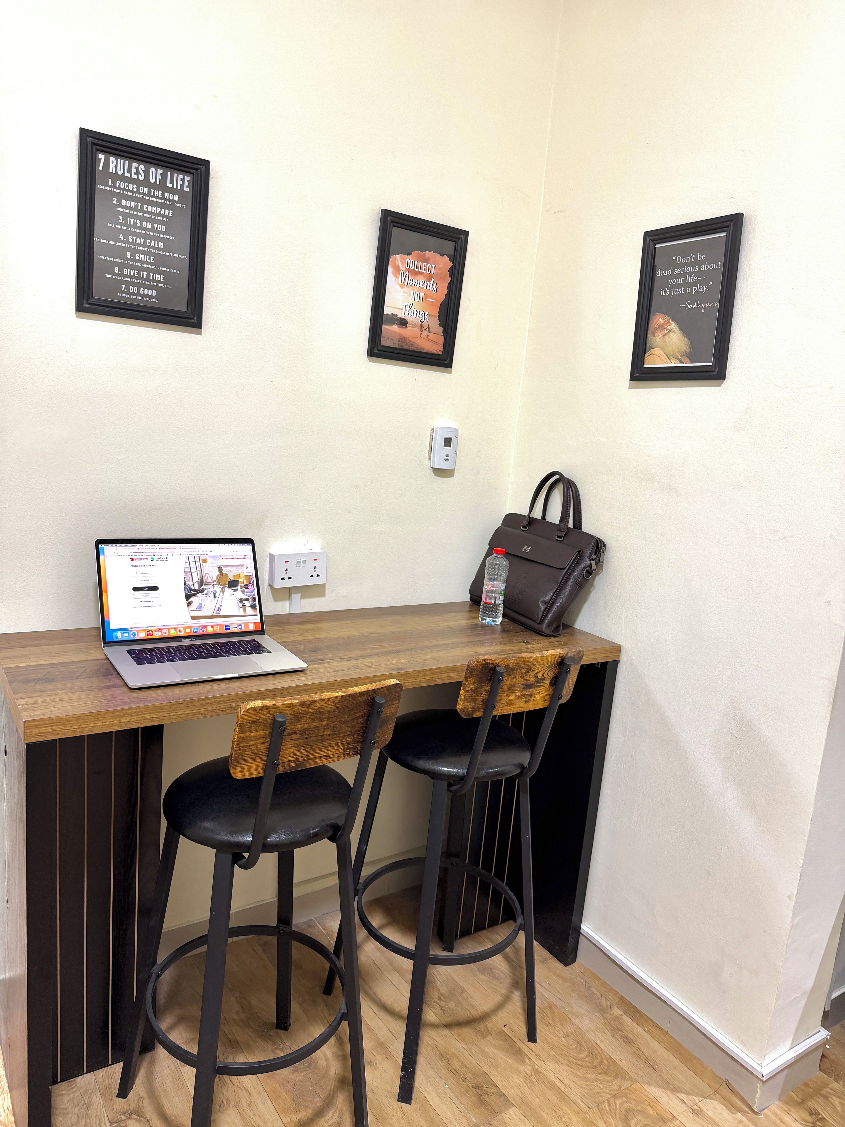 Um espaço de trabalho com laptop, duas cadeiras, uma mesa e cartazes motivacionais na parede.