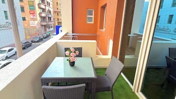 Varanda com grama sintética, uma mesa, cadeiras e um vaso de flores.