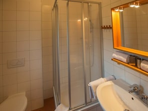 Casa de banho com cabine de chuveiro envidraçada, lavatório com espelho e sanita.