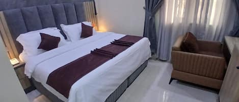 Quarto de hotel com uma cama grande, um sofá e uma janela com cortinas.