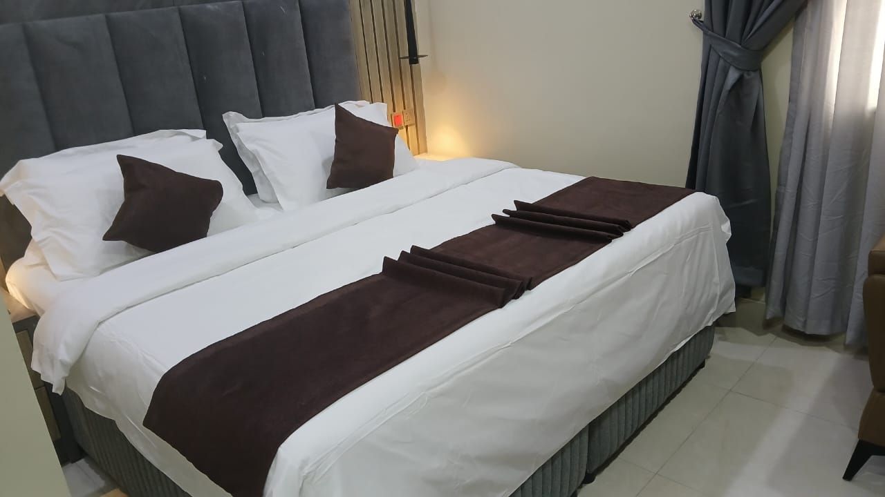 Cama bem arrumada com lençóis brancos e castanhos, cabeceira e mesa de cabeceira com abajur.
