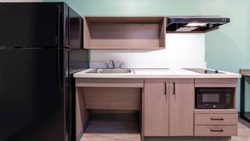 Cozinha compacta com geladeira preta, pia com torneira dupla, micro-ondas e armários de madeira.