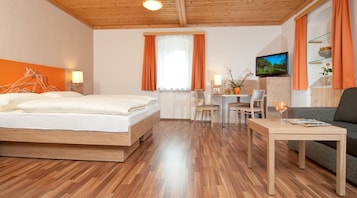 Quarto de hotel com cama, escrivaninha, poltrona, sofá e televisão.
