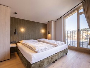 Quarto com cama, duas luminárias de cabeceira, janela com vista e piso de madeira.
