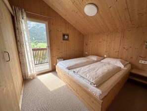 Quarto de madeira com duas camas, uma janela com cortinas e vista para uma paisagem de montanha.