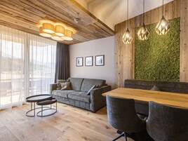 Um espaço de estar moderno com teto de madeira, parede verde, sofá, mesa de jantar e luminárias pendentes.