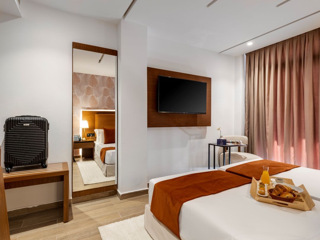 Quarto de hotel com cama, televisão de tela plana, escrivaninha com abajur e bandeja de café da manhã.