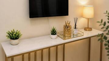 Bancada de recepção com televisão de tela plana montada acima, luminária de mesa e objetos decorativos, incluindo uma pequena planta e um objeto dourado.