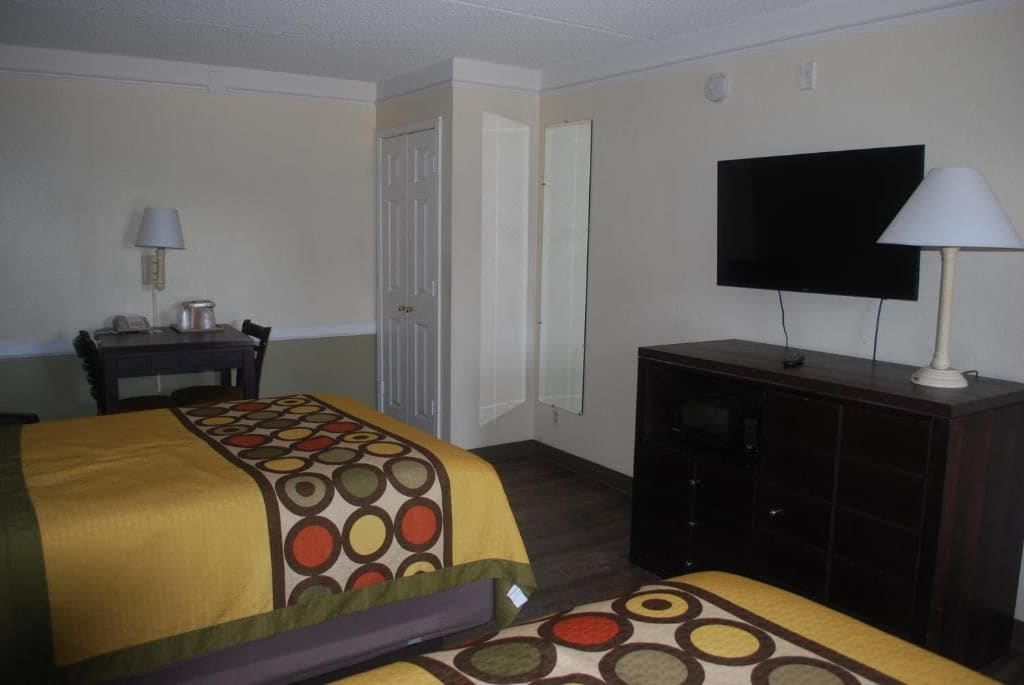 Quarto de hotel com cama, escrivaninha, televisão e armário.
