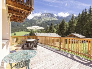 Um deck de madeira com mesa e cadeiras, com vista para uma paisagem montanhosa.